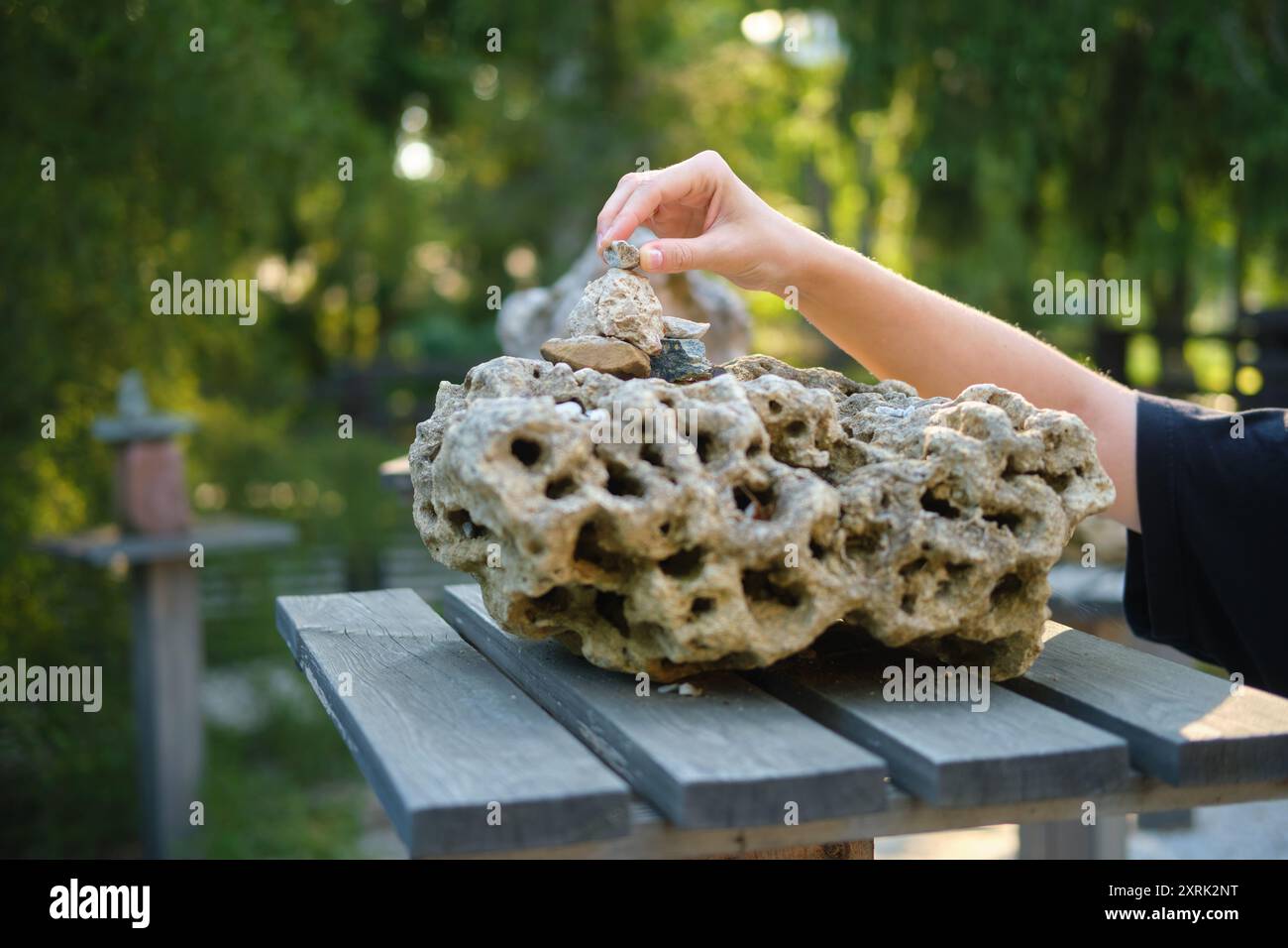 Hand placing a small stone on a large porous rock on a wooden pedestal ...