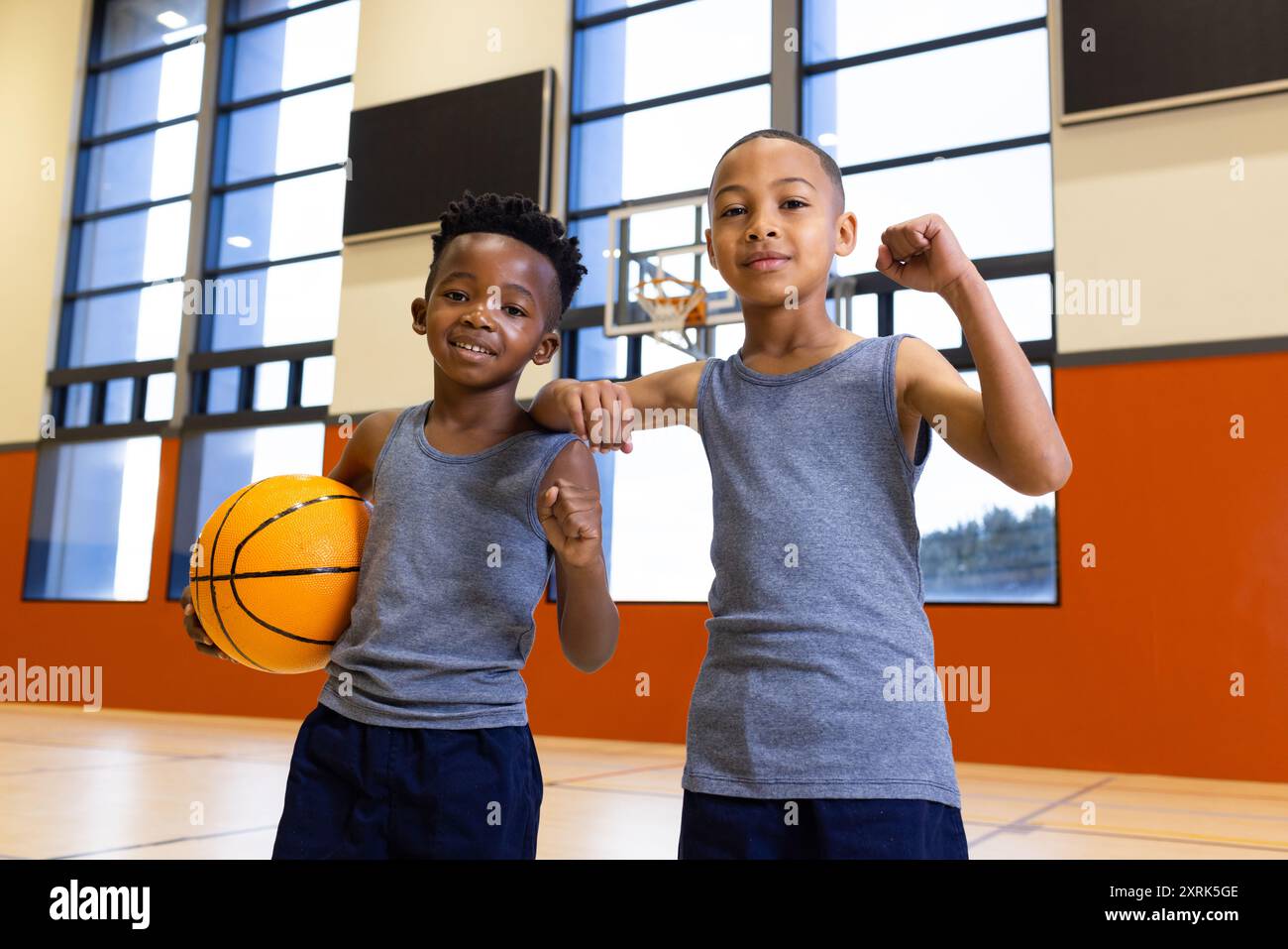 In school gym, boys holding basketball and flexing muscles, smiling ...