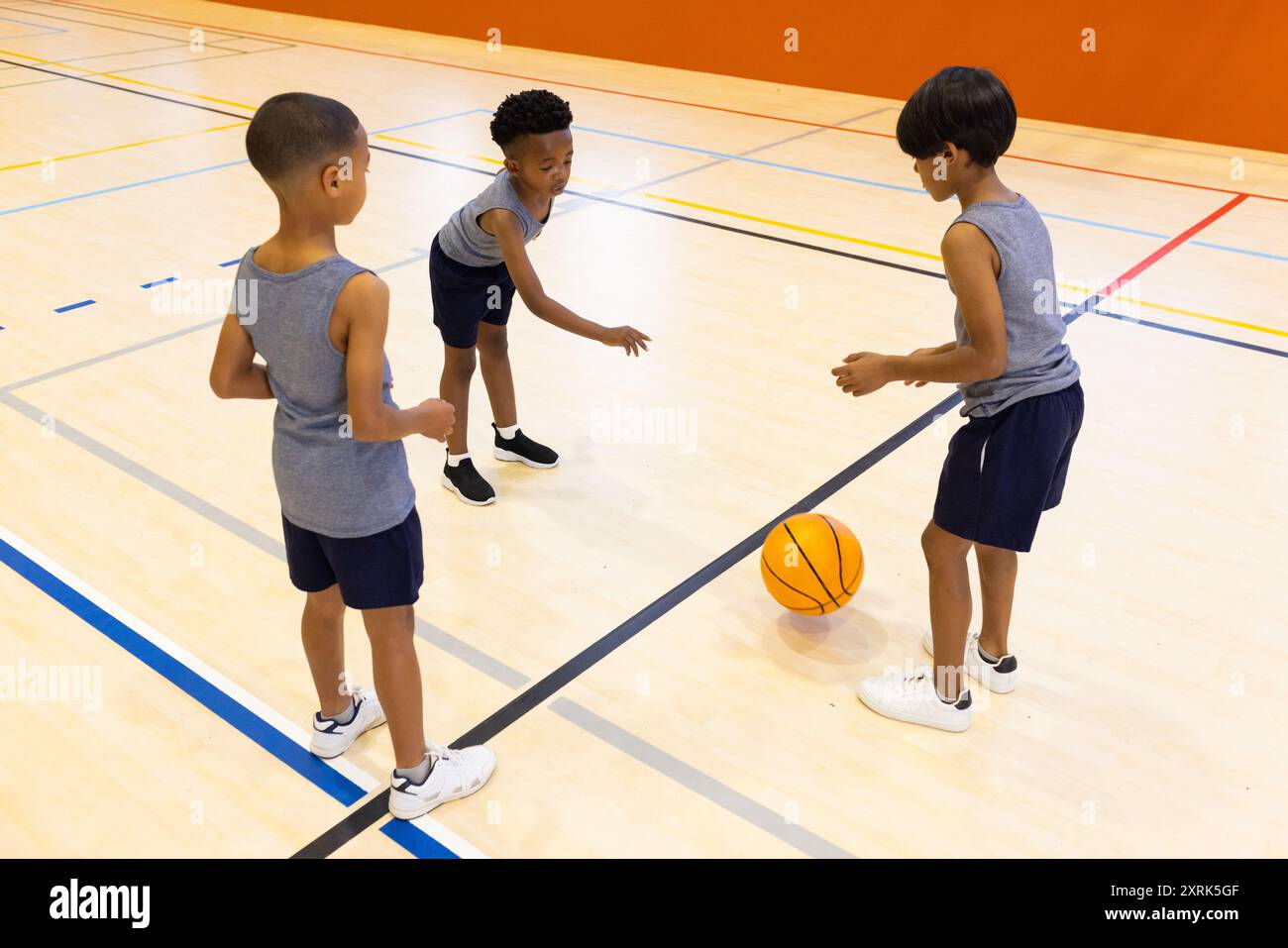 Playing basketball in school gym, three boys practicing dribbling and ...