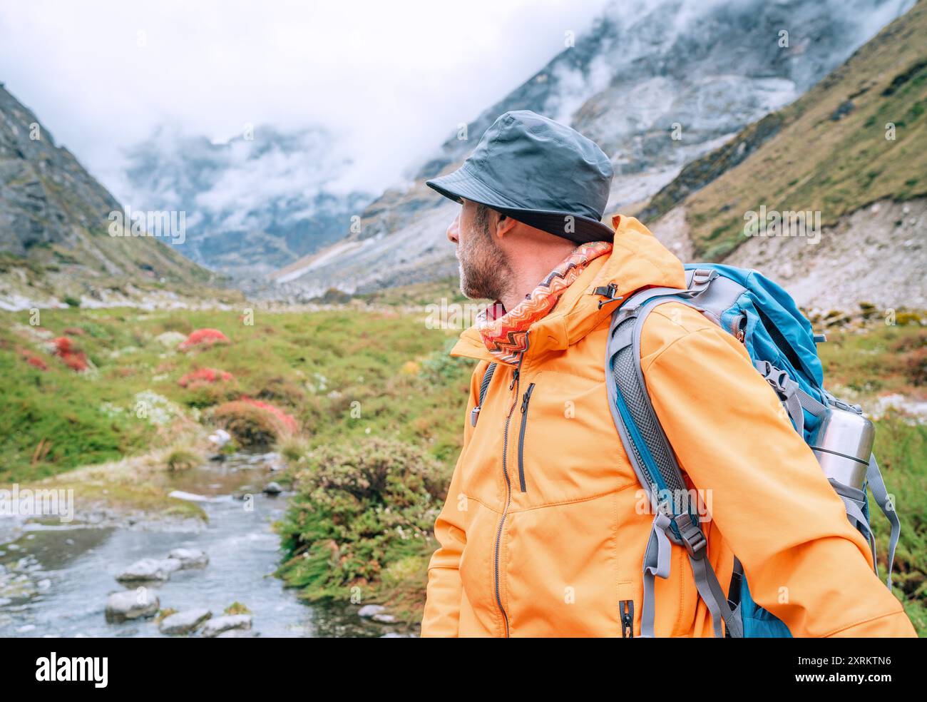Man with backpack dressed orange waterproof jacket turning back ...