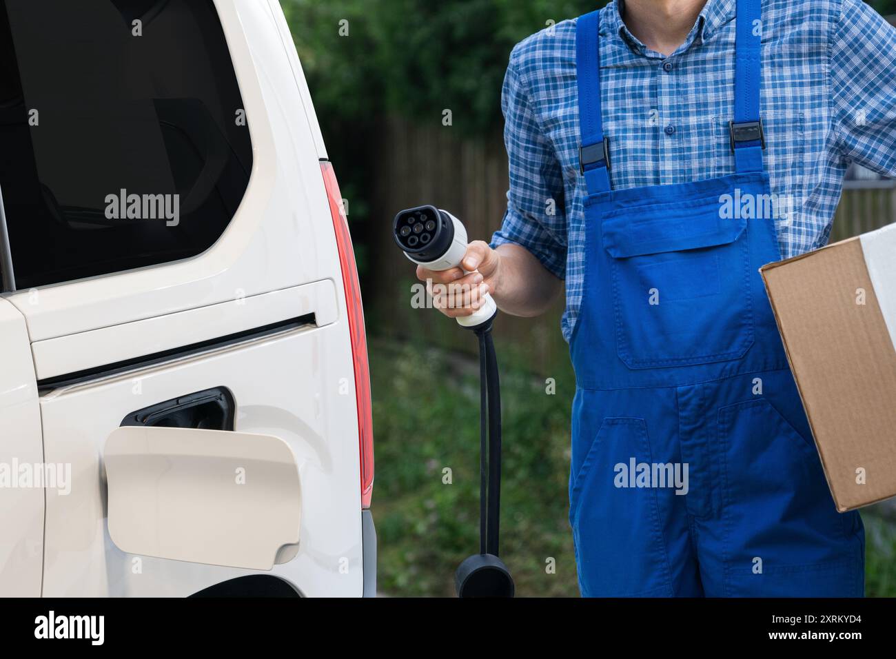 Delivery man in uniform holds electric vehicle charging plug next to ...