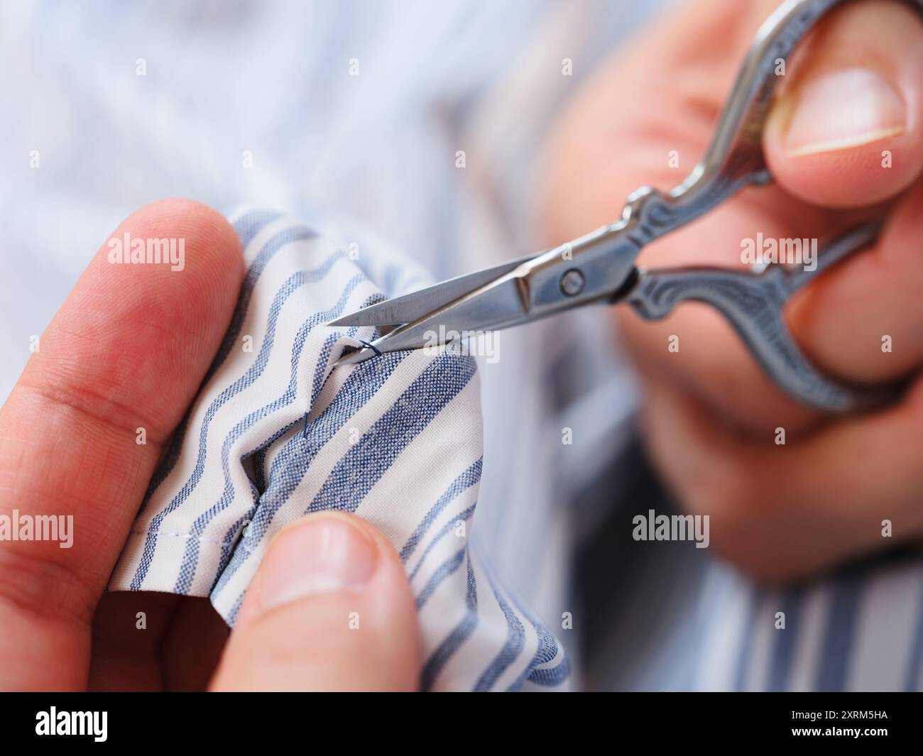 A woman hands with scissors cutting open the basting stitch on the ...