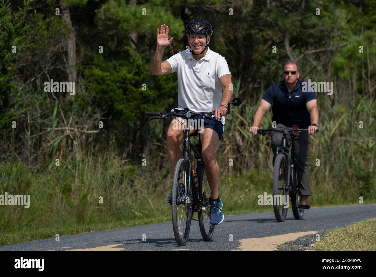 President Joe Biden waves to a cheering crowd as he rides his bike ...