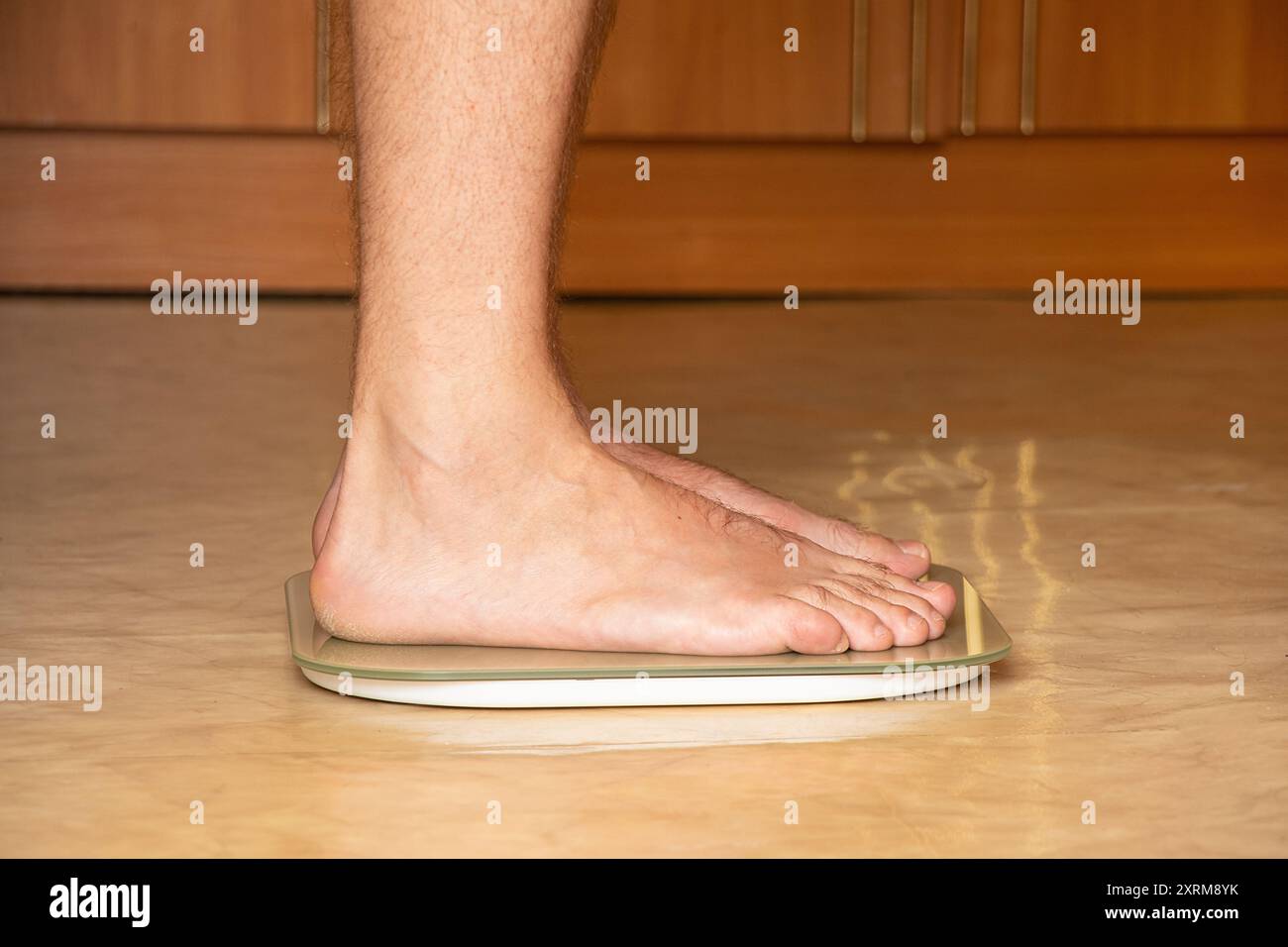 A man stands on a floor scale on the floor in an apartment, monitoring ...