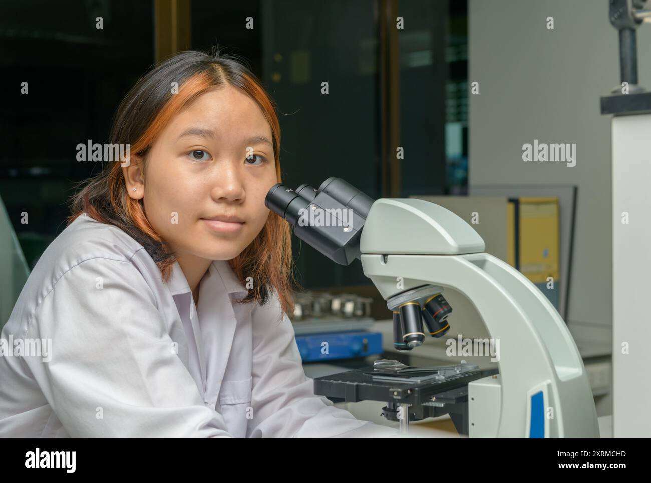 Cute scientist schoolgirl in lab coat is using microscope for study microbiology in laboratory ...