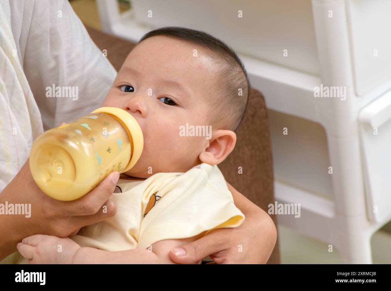 A portrait of cute newborn baby being fed by her mother using bottle ...