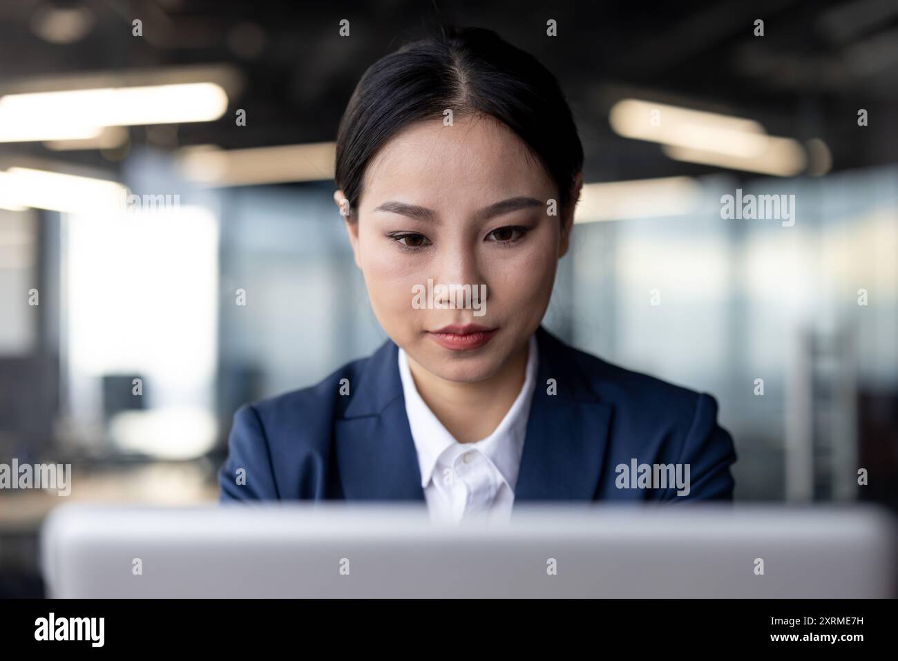 Asian businesswoman in a suit deeply focused on her laptop screen in a ...