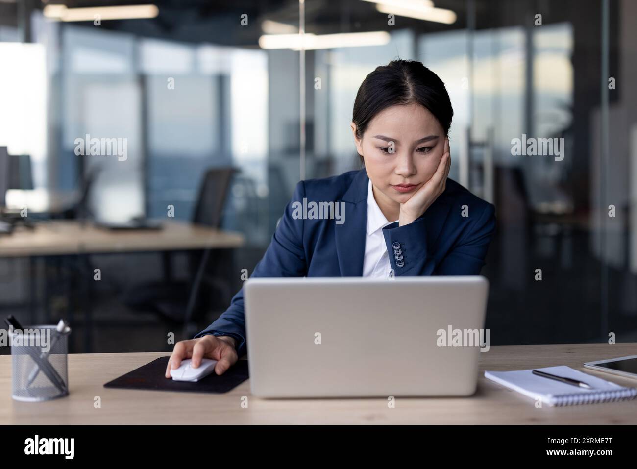 Asian businesswoman focused on her laptop while working in a contemporary office environment ...