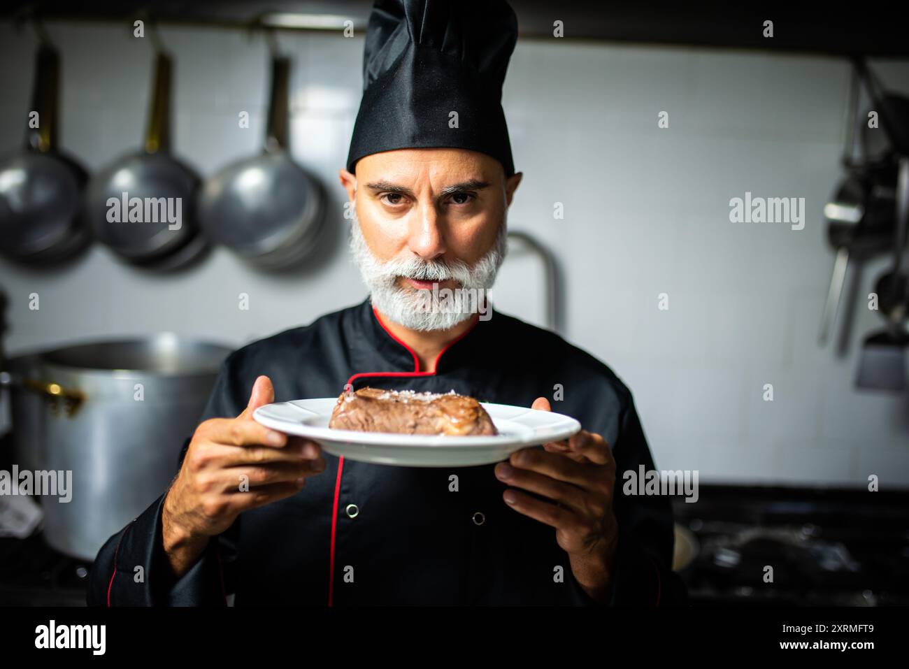 Professional chef with a long beard wearing black uniform, holding a ...