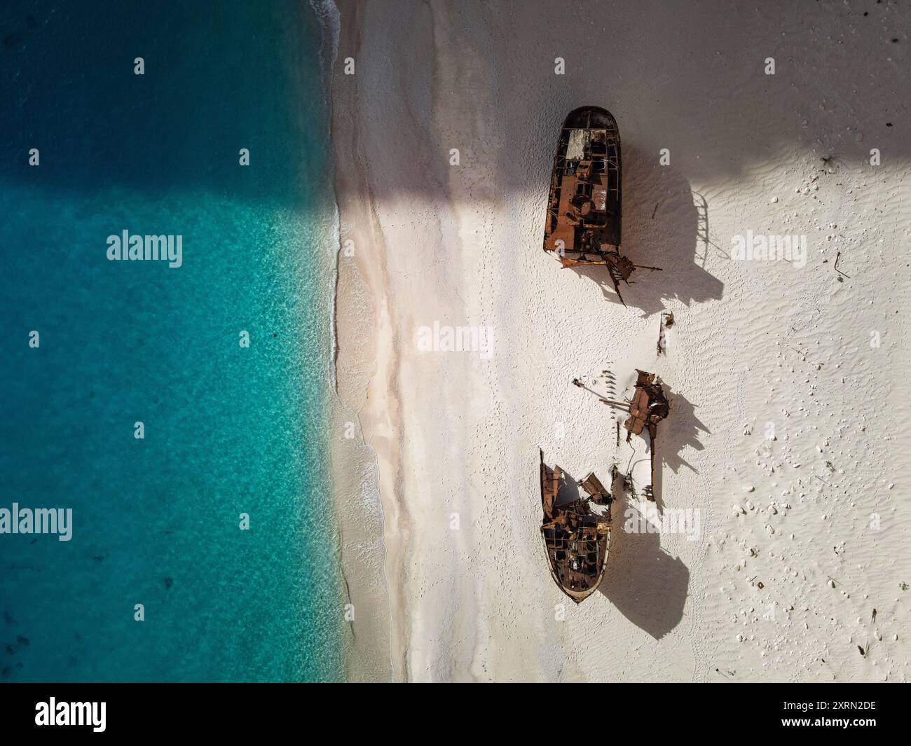 Aerial view of a shipwreck on a sandy beach with clear blue water ...