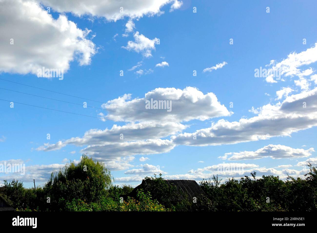 Fluffy white clouds float across a bright blue sky, casting shadows ...