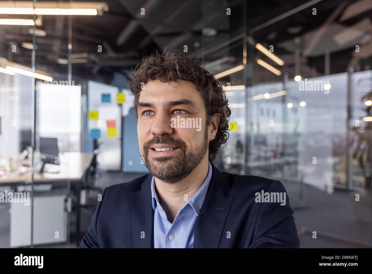 Confident businessman smiling in modern office with glass walls and ...