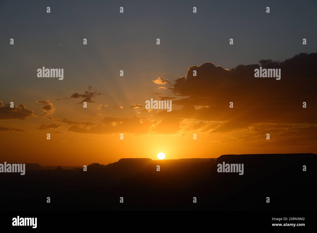 Orange sunrays radiate from setting sun as it touches a ridge beneath ...