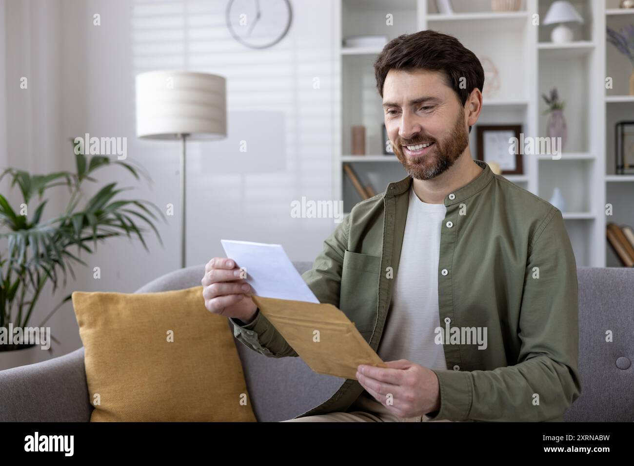 Man sitting on couch opening letter with smile and joy. Happy recipient ...
