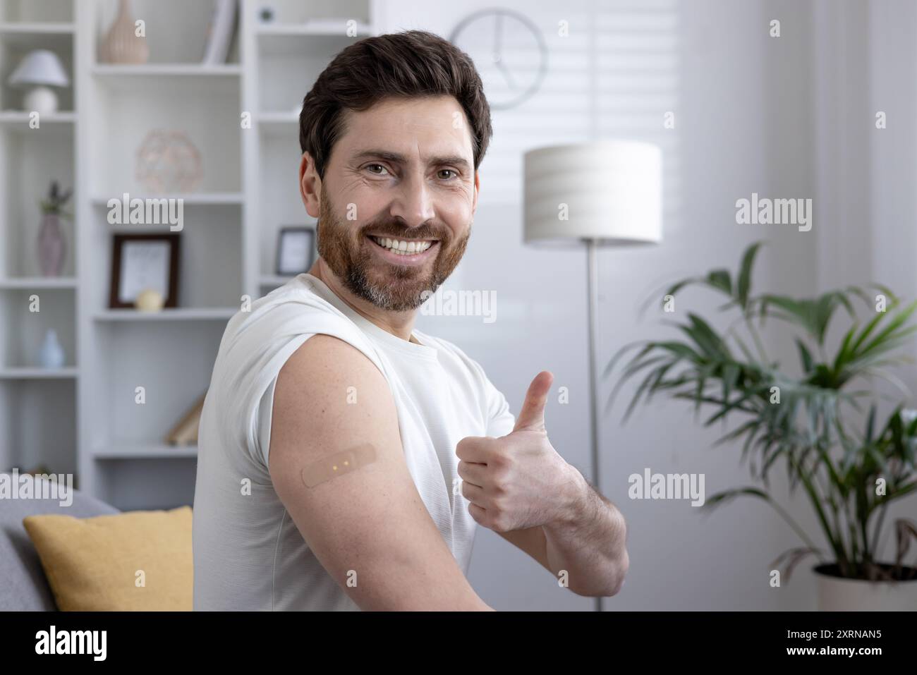 Smiling man with beard at home after vaccination showing bandage on arm ...
