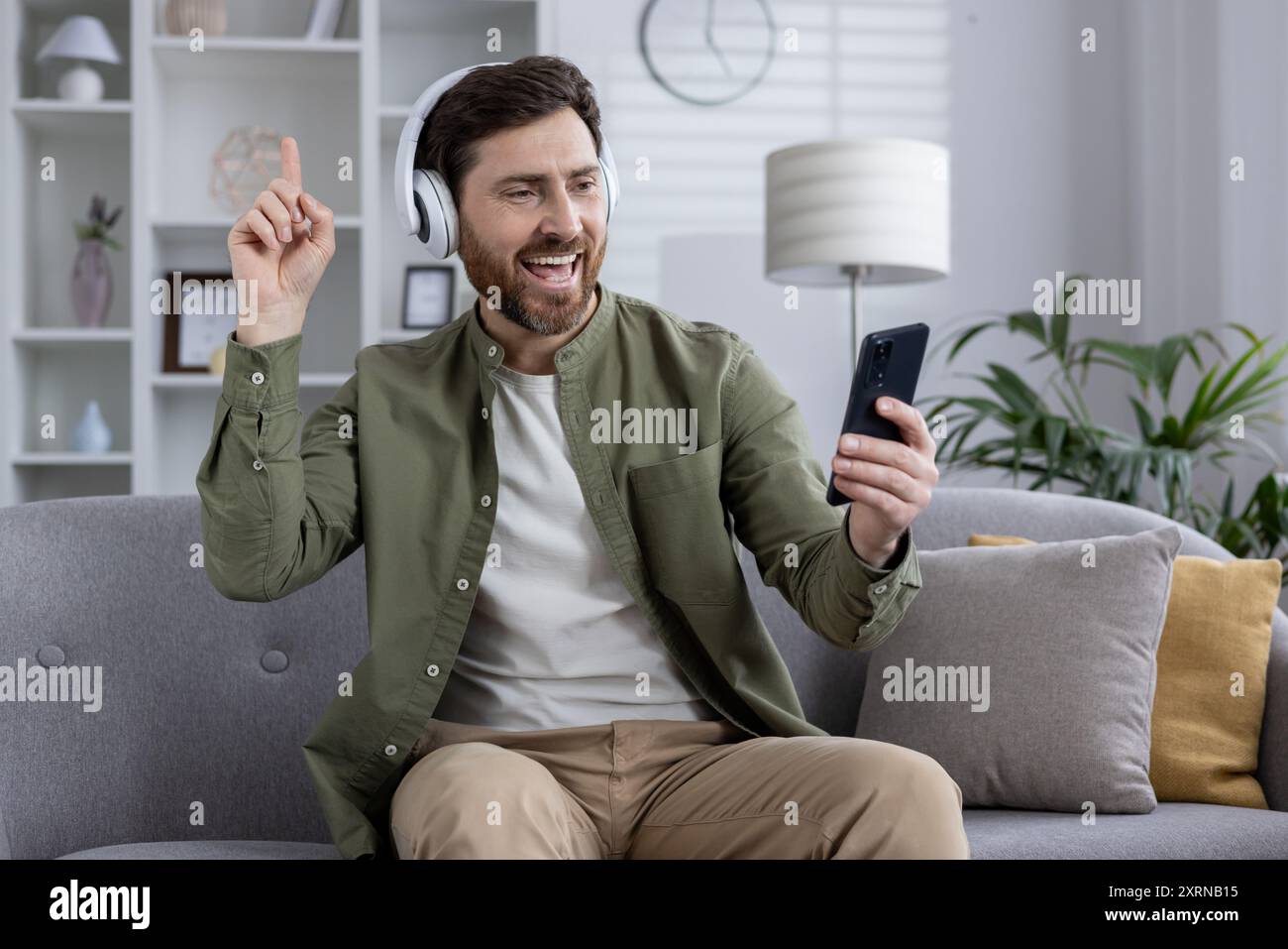 Man wearing headphones holding phone, smiling and pointing while ...