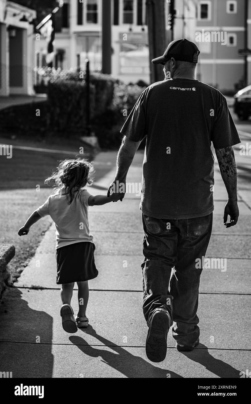 Little girl and her daddy walk down a city street hand in hand. Knowing ...