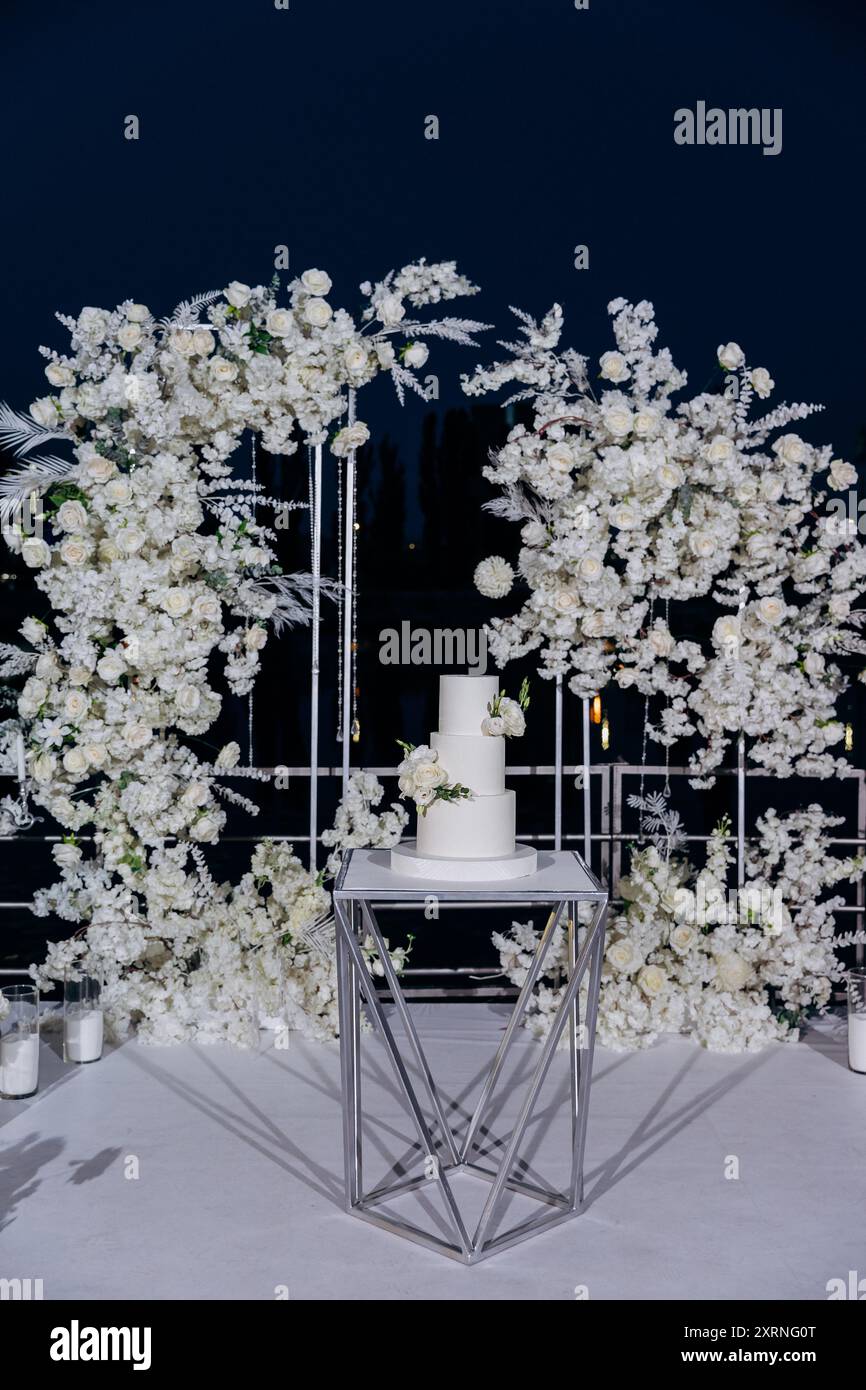 Wedding setup with three-tier white cake with floral accents. Wedding ...