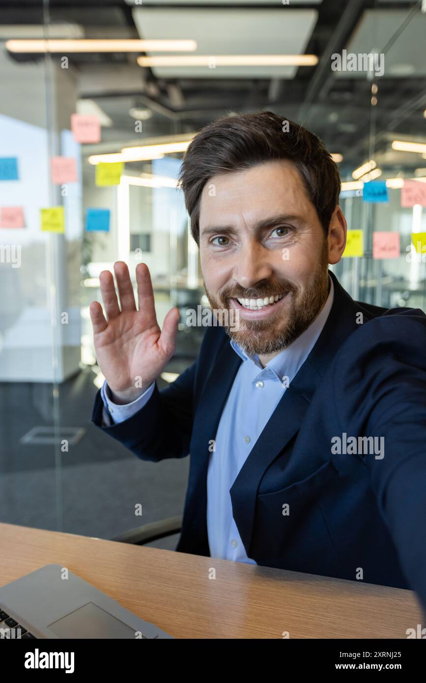 Smiling businessman waving hand during video call in office ...