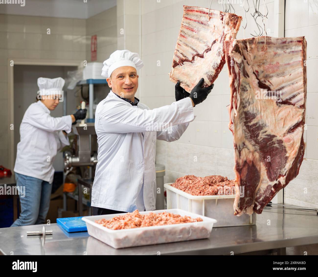 Diligent male butcher showing big piece of beef ribs in meat section of ...