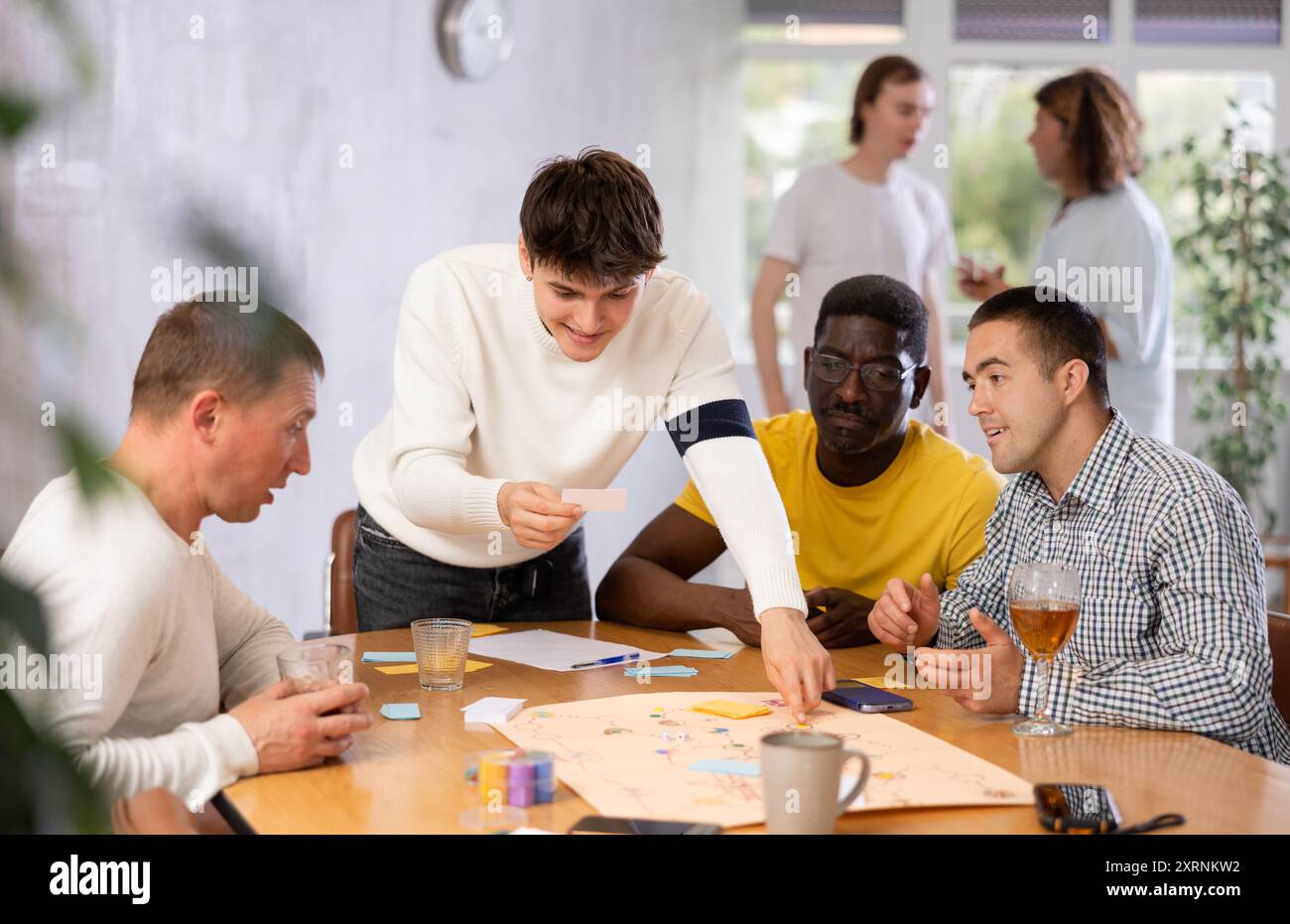 Group of enthusiastic men playing board game sitting around table Stock ...