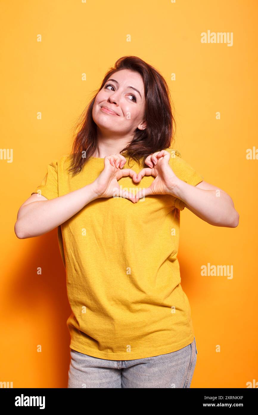 Smiling woman makes a heart shape with her fingers on her chest ...