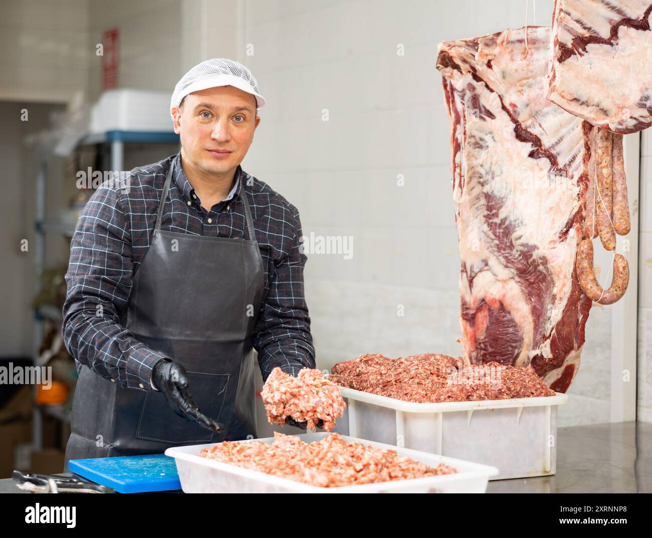 Positive male butcher making ground beef in butcher shop Stock Photo ...