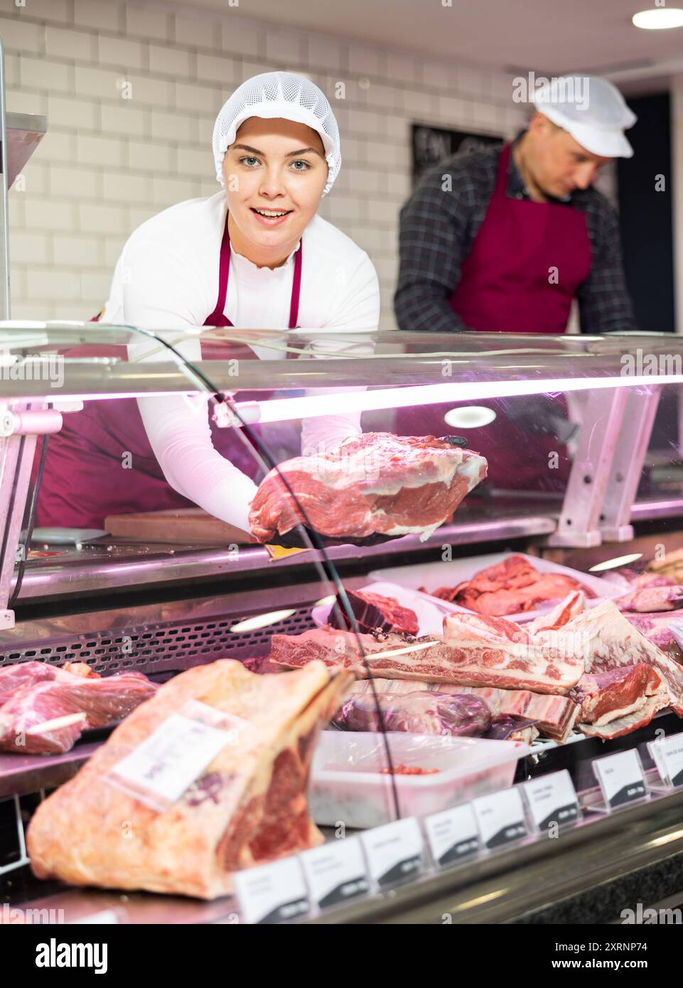 Smiling female butcher offering to sell big piece of beef in butcher ...