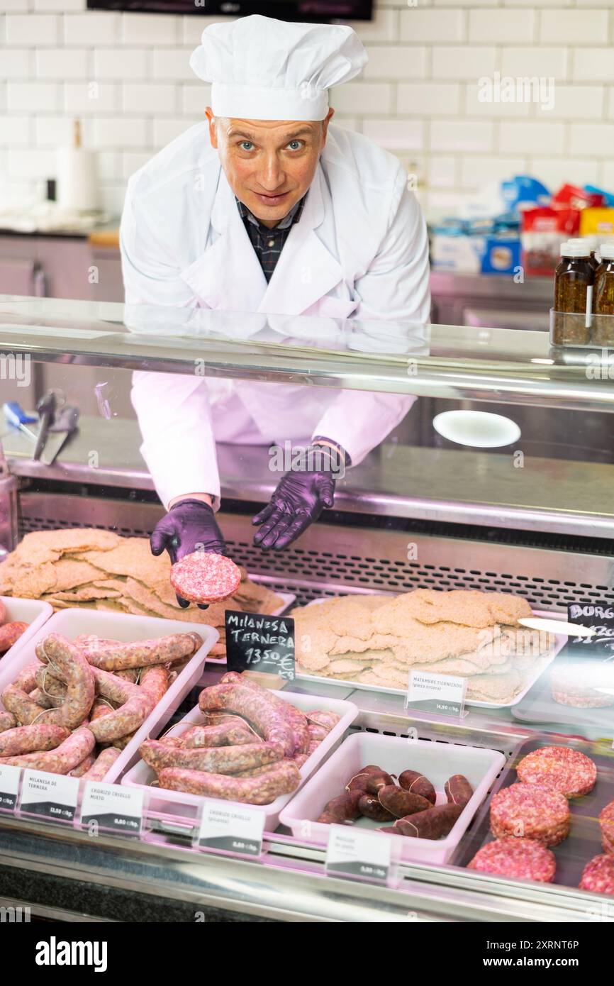 Diligent female butcher showing beef burger patties in butcher shop ...