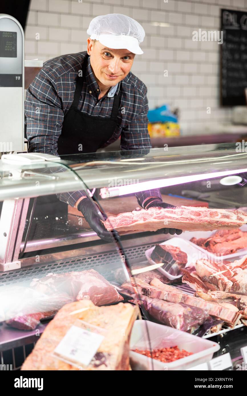Adult man puts beef ribs in showcase Stock Photo - Alamy