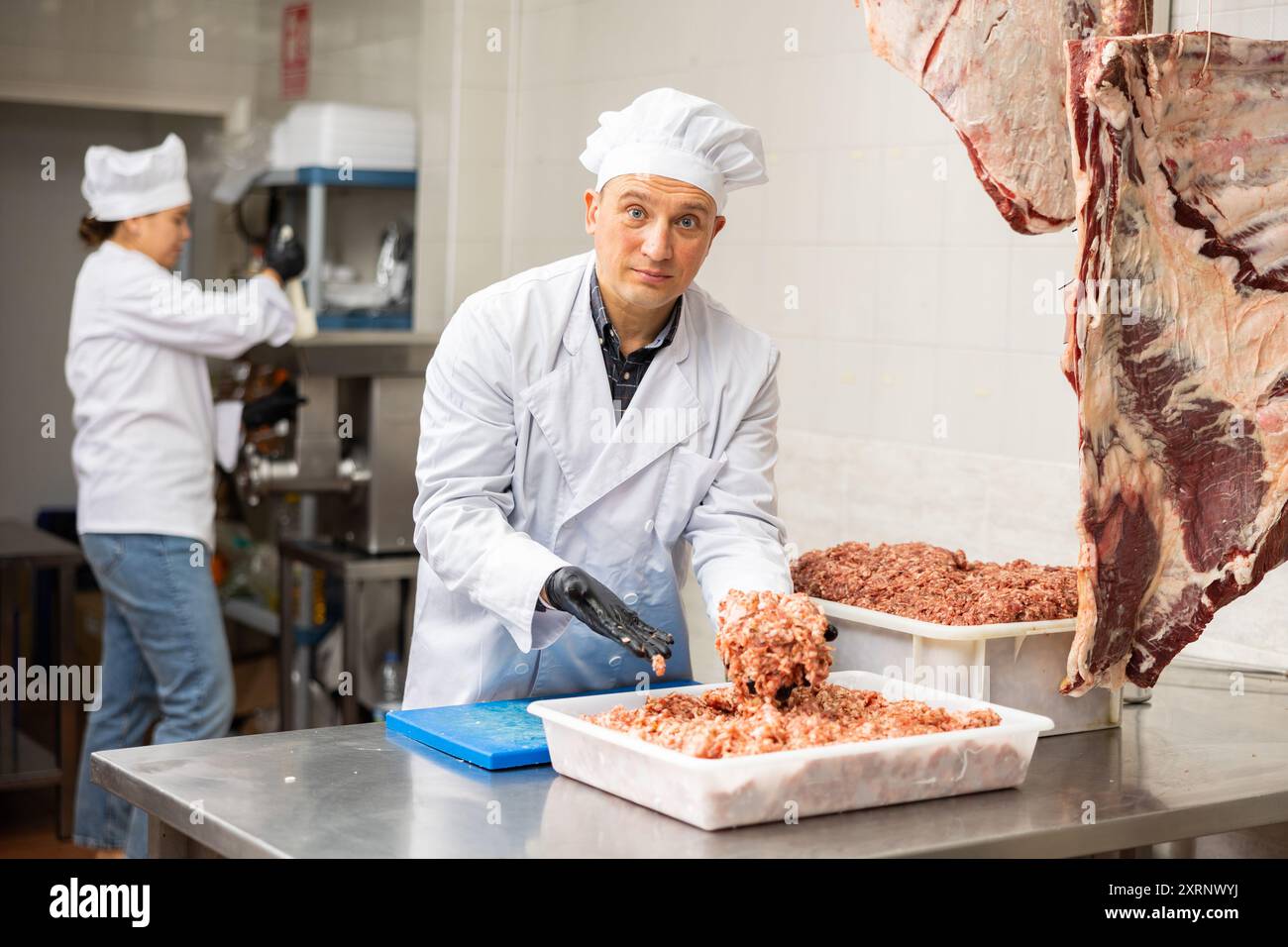 Positive male butcher making ground beef in butcher shop Stock Photo ...