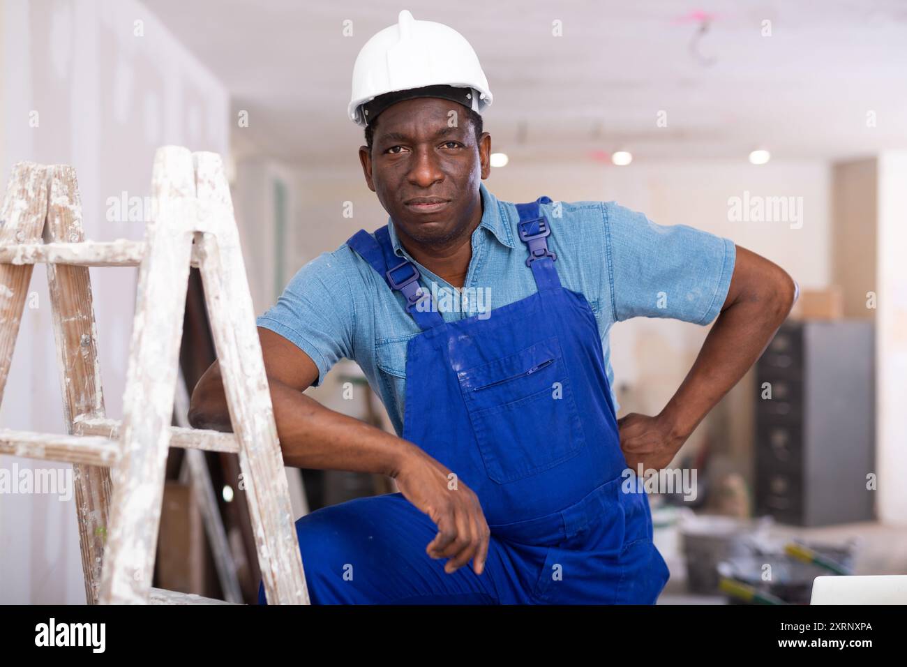 Portrait of confident african-american worker in blue overalls in room ...
