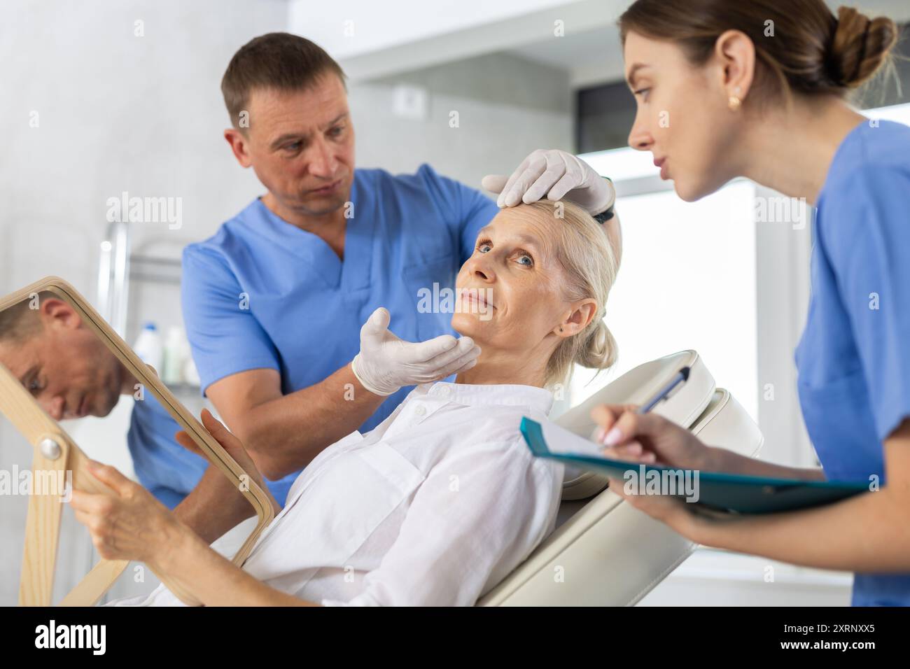 Man dermatologist examines skin of senior womans face, female nurse ...