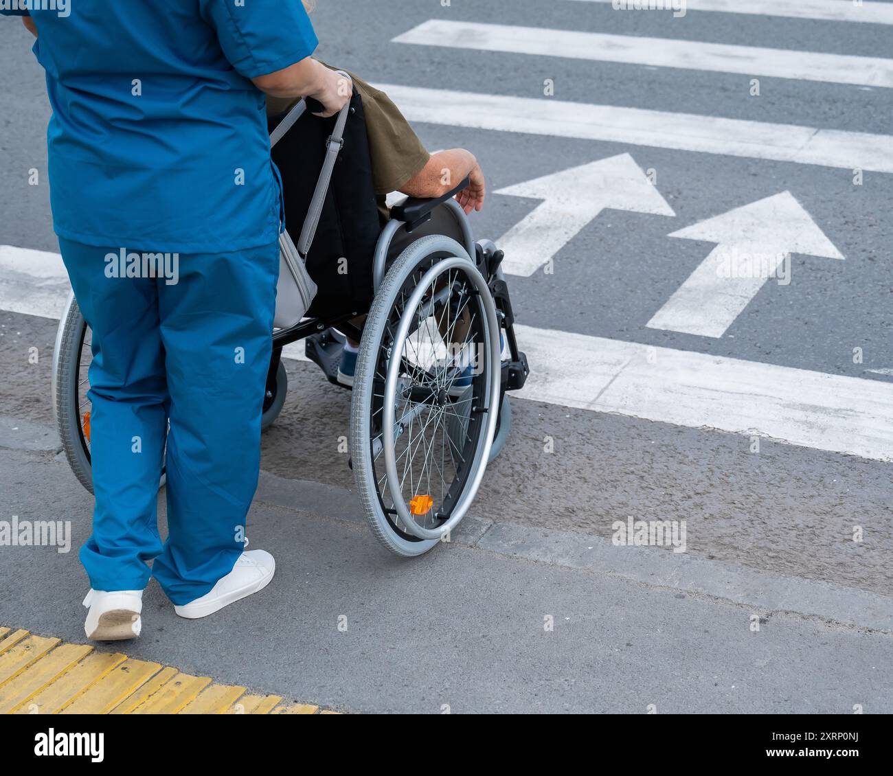 Rear view of a nurse helping an elderly woman in a wheelchair cross the ...