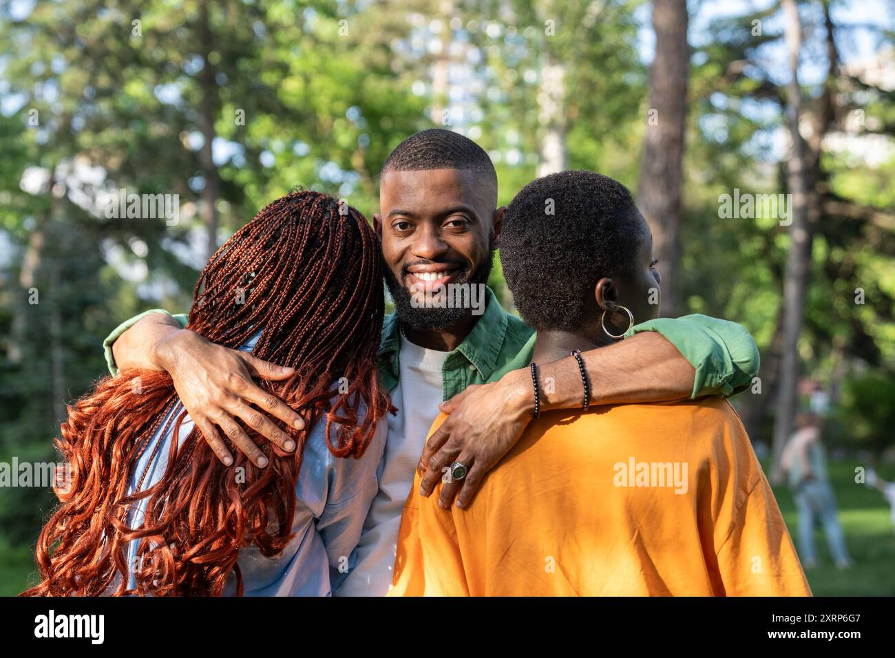 Smiling African American man hugs friends girls who standing with their ...