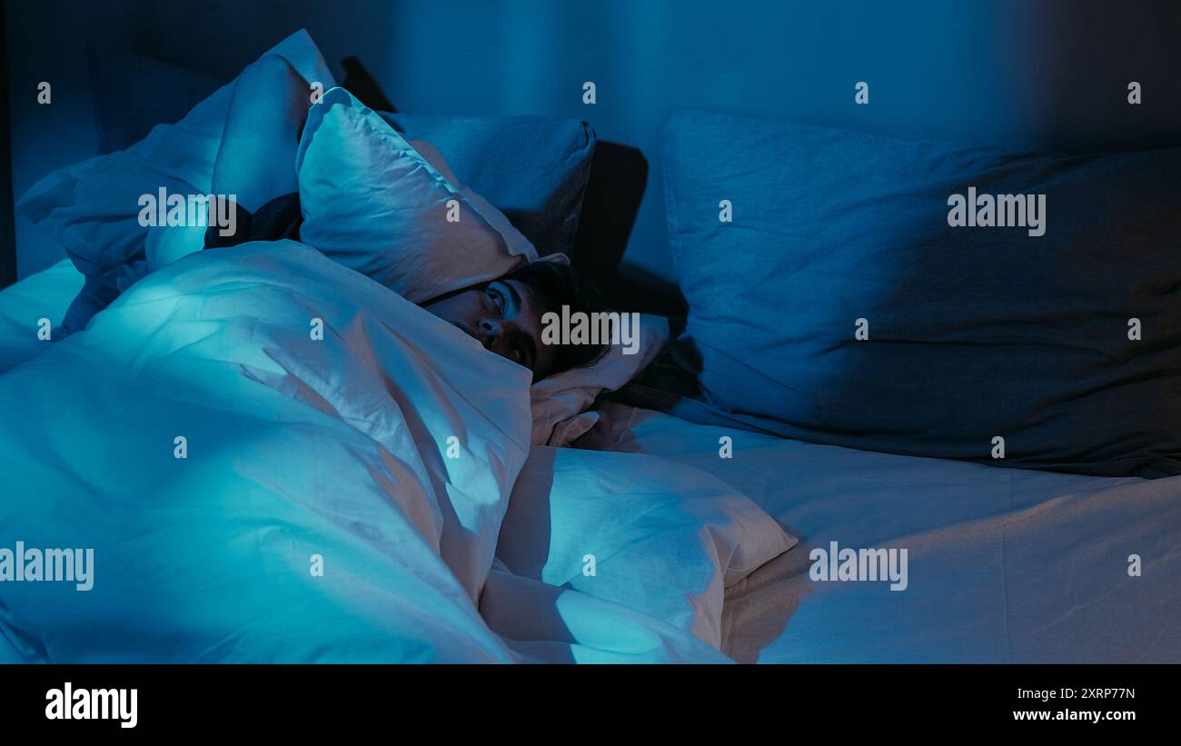 Pensive man trouble sleeping disturbed in bed with soft pillows under ...