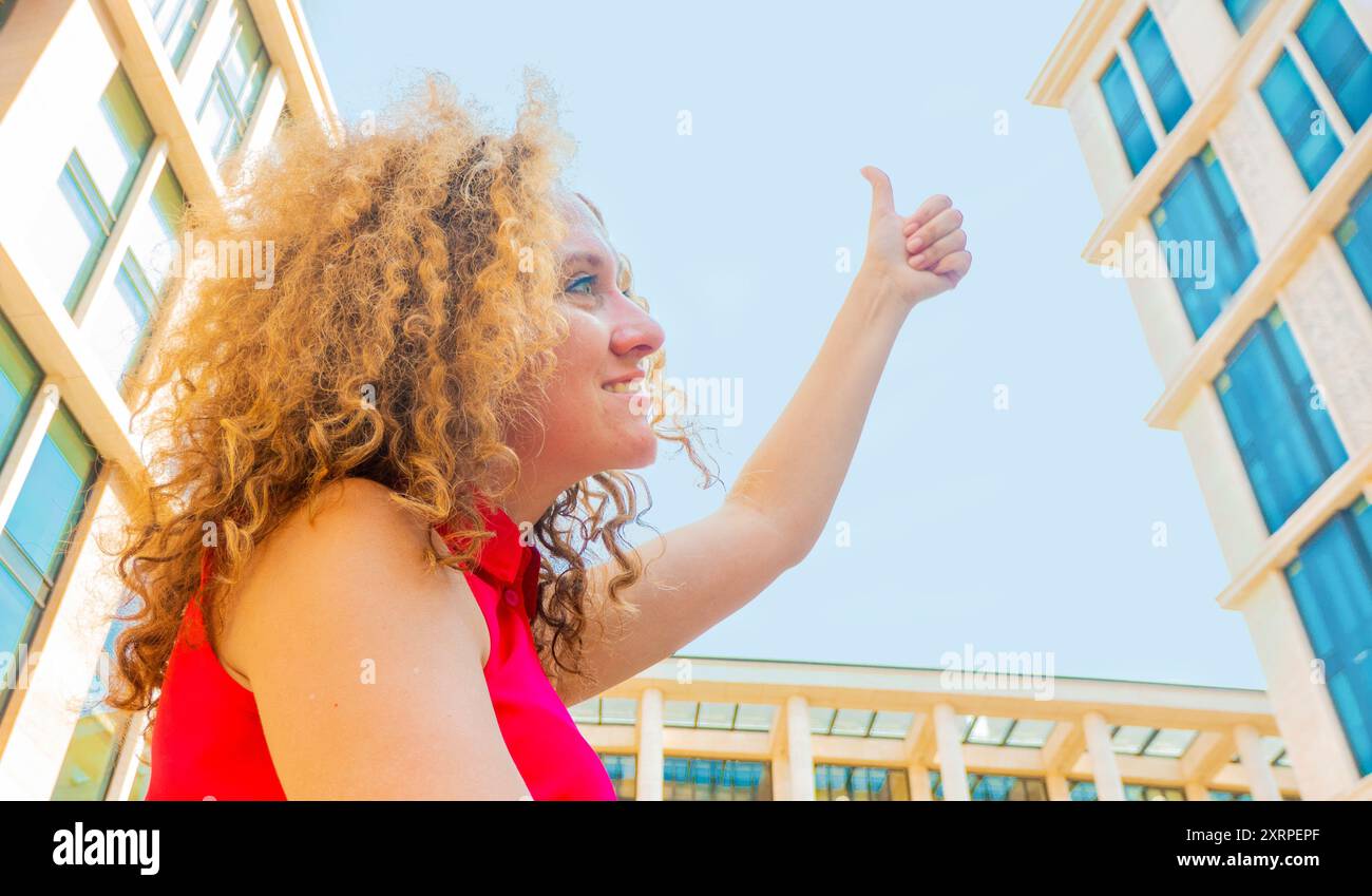 Portrait happy fasion woman shows thumb up against the sky and looking ...