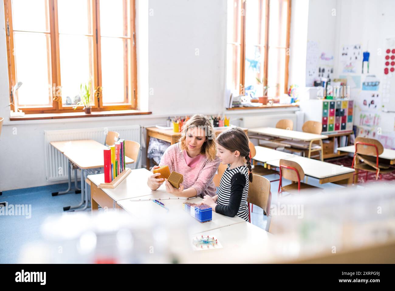 Hardworking teacher learning with young schoolgirl in classroom ...