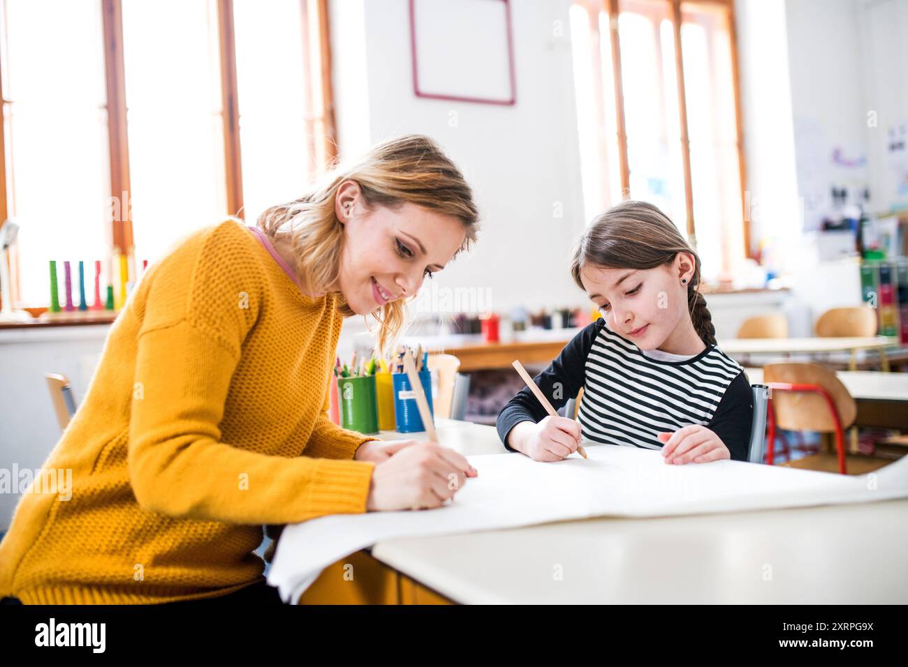 Hardworking teacher learning with young schoolgirl in classroom ...