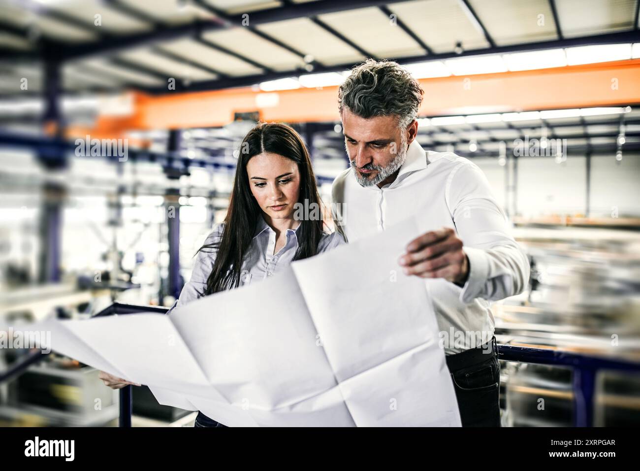 Two project managers standing in modern industrial factory, looking ...