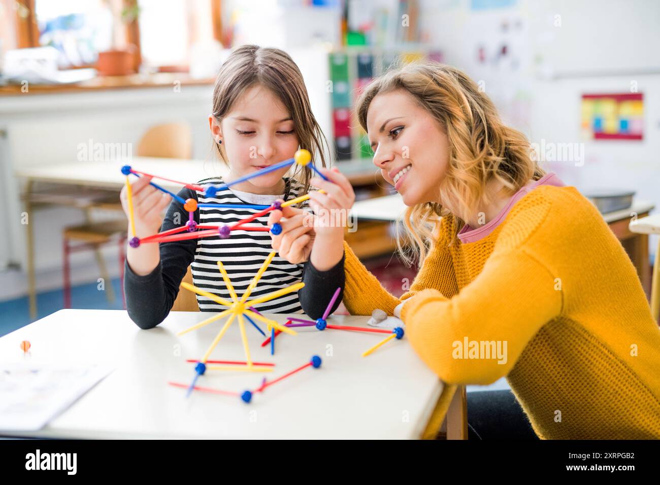Hardworking teacher learning with young schoolgirl in classroom ...
