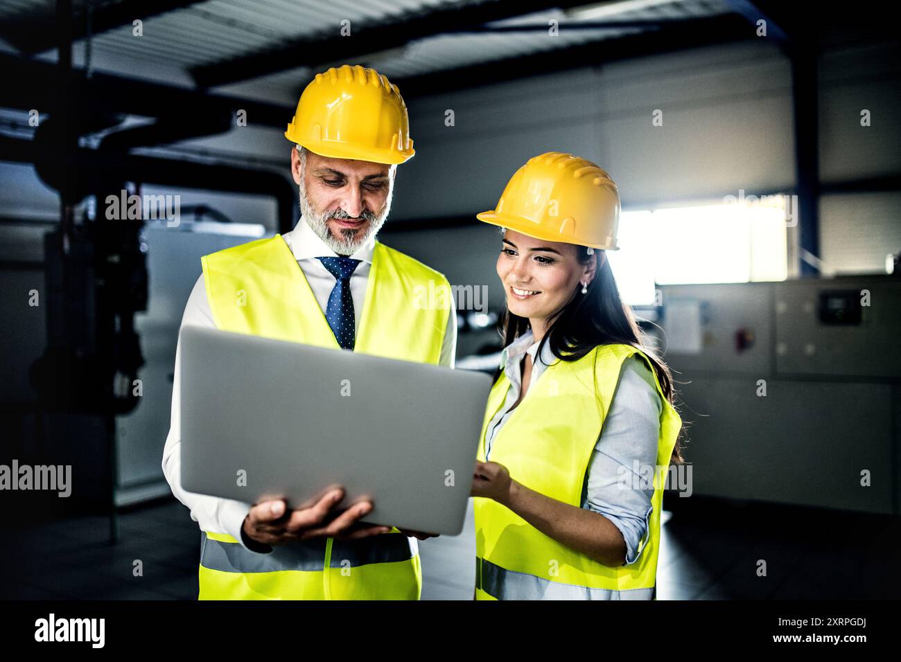 Two project managers standing in modern industrial factory, looking at ...