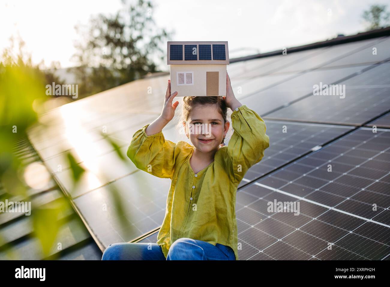 Cute girl holding model of house with solar panels, sitting on rooftop ...