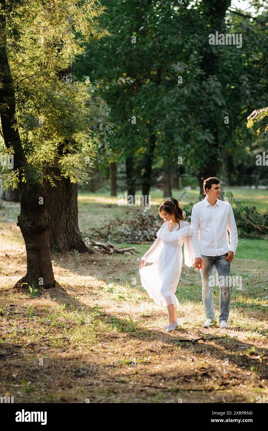 guy and a girl walk along the paths of a forest park between tall trees ...