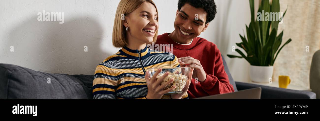 A multicultural couple laughs together while enjoying a movie night at ...