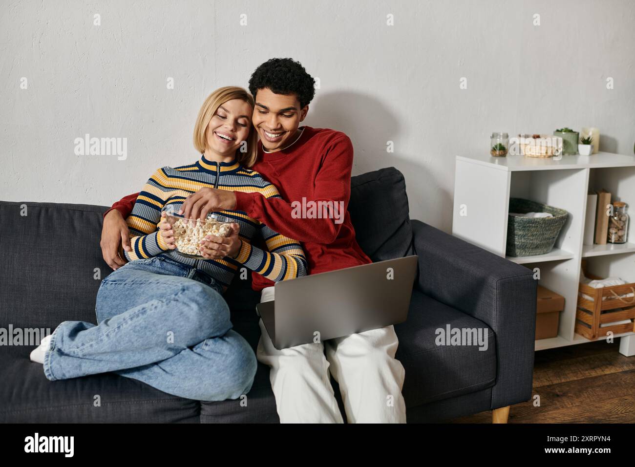A multicultural couple enjoys a movie night at home, sharing popcorn ...