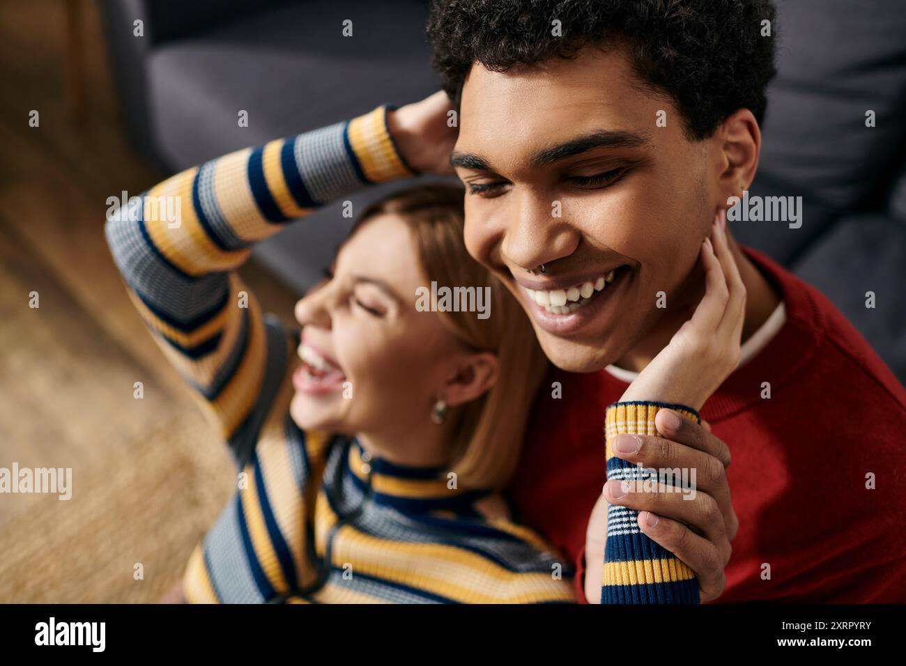 A happy, multicultural couple laughs together in their modern apartment ...