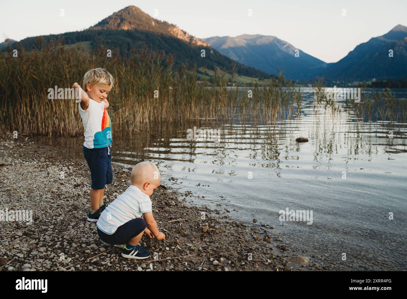 Adorable young children throwing stones in water at lake by mountains ...