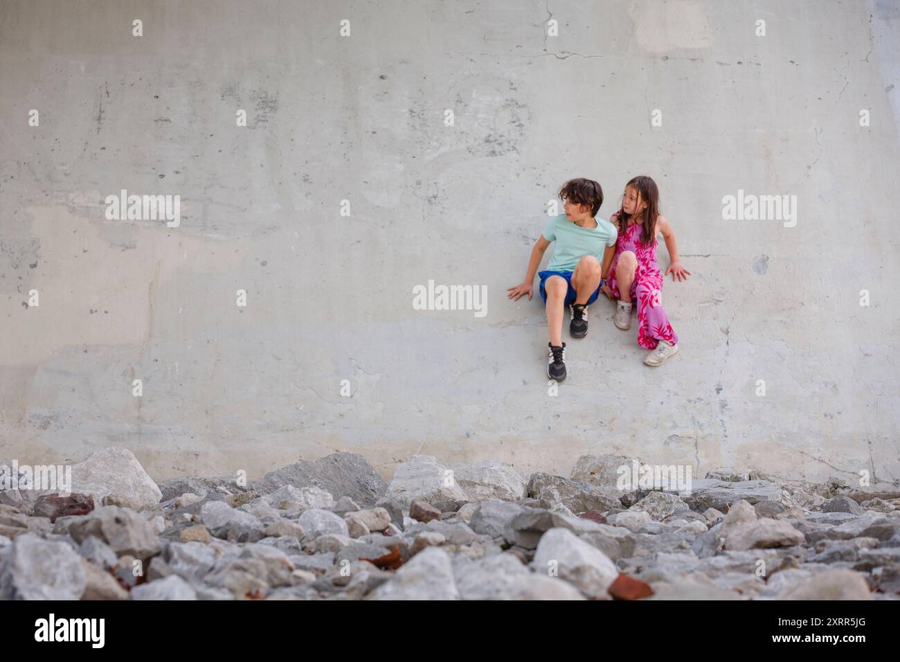 Two children sit on sloped cement wall in barren, urban landscape Stock ...