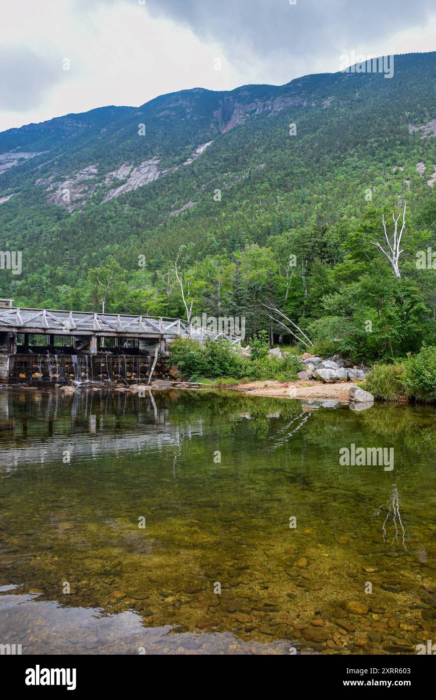 Wooden bridge and dam over a calm river with mountainous backdrop Stock ...